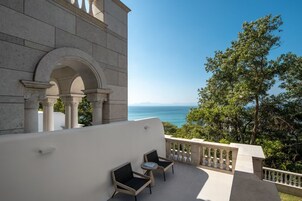 Uma varanda com duas cadeiras e uma mesa, com vista para o mar e um horizonte montanhoso.
