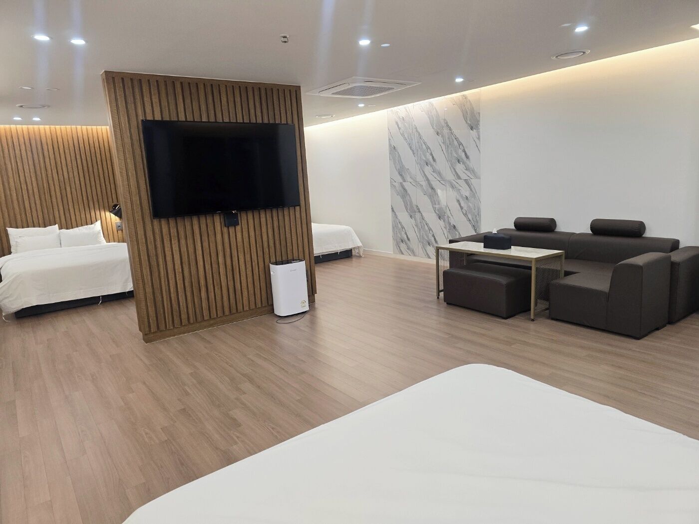 Quarto de hotel moderno com cama, sofá, televisão e parede de mármore.