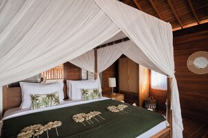 Uma cama com dossel, almofadas com estampas de palmeiras e um edredom verde com motivos florais.