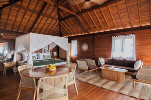 Um quarto amplo com teto de madeira, cama com dossel, sofá, mesa de centro e cadeiras de vime.
