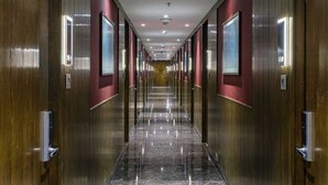 Um corredor longo e estreito com painéis de madeira e detalhes vermelhos, que leva a uma porta no final.