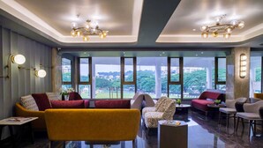 Um lobby de hotel moderno com área de estar em curva, grandes janelas com vista para a cidade e luminárias contemporâneas.
