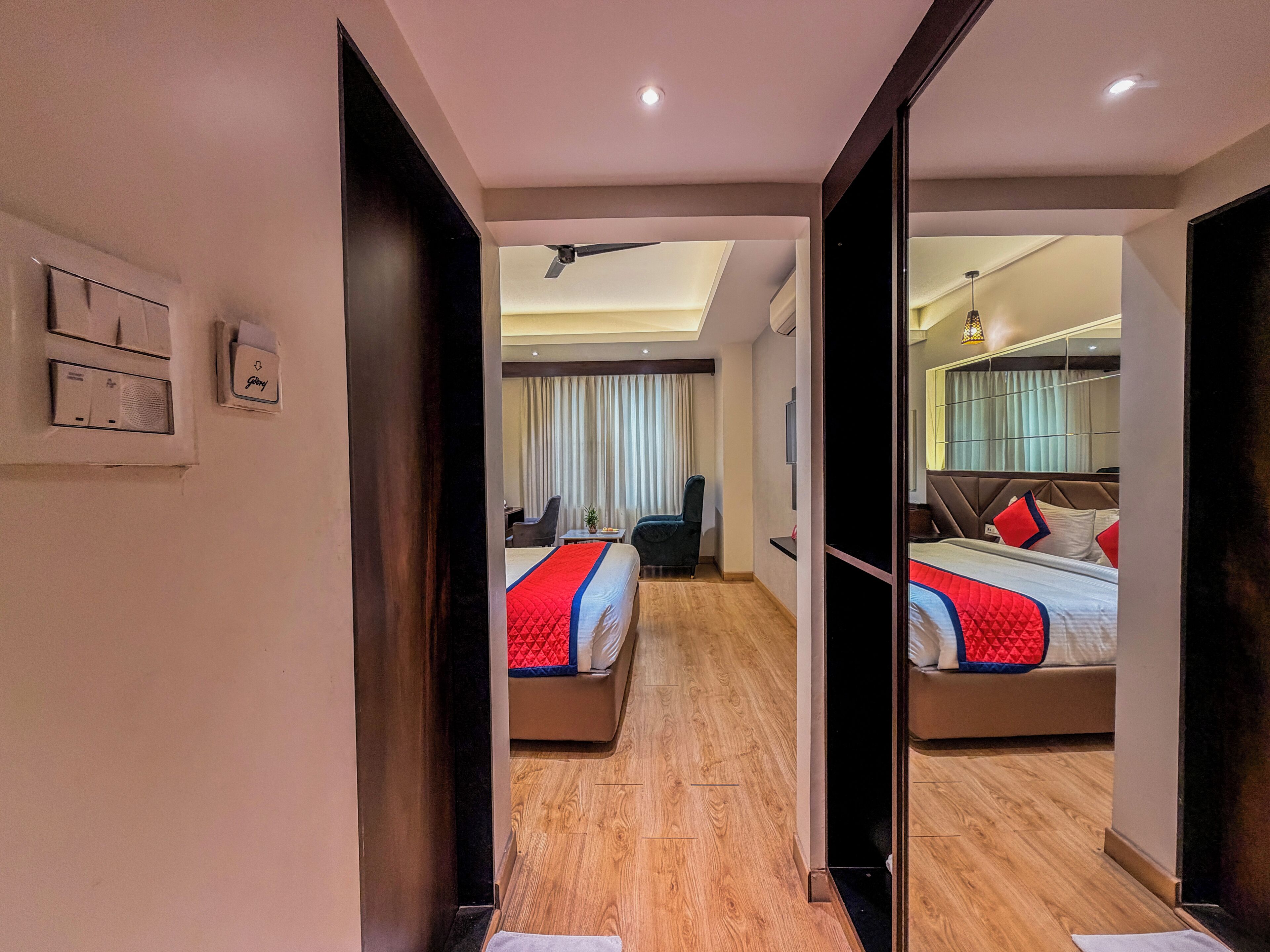 Quarto de hotel com armário espelhado, cama com colcha vermelha e azul, escrivaninha e uma cadeira.