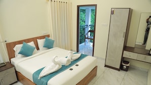 Uma cama bem arrumada com cabeceira de madeira, mesa de cabeceira, guarda-roupa e uma varanda visível através de uma porta aberta.