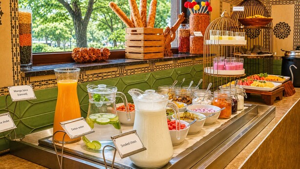 Buffet com diversas opções de comida e bebida, incluindo chicharrones defumados, suco de manga e um jarro de leite.