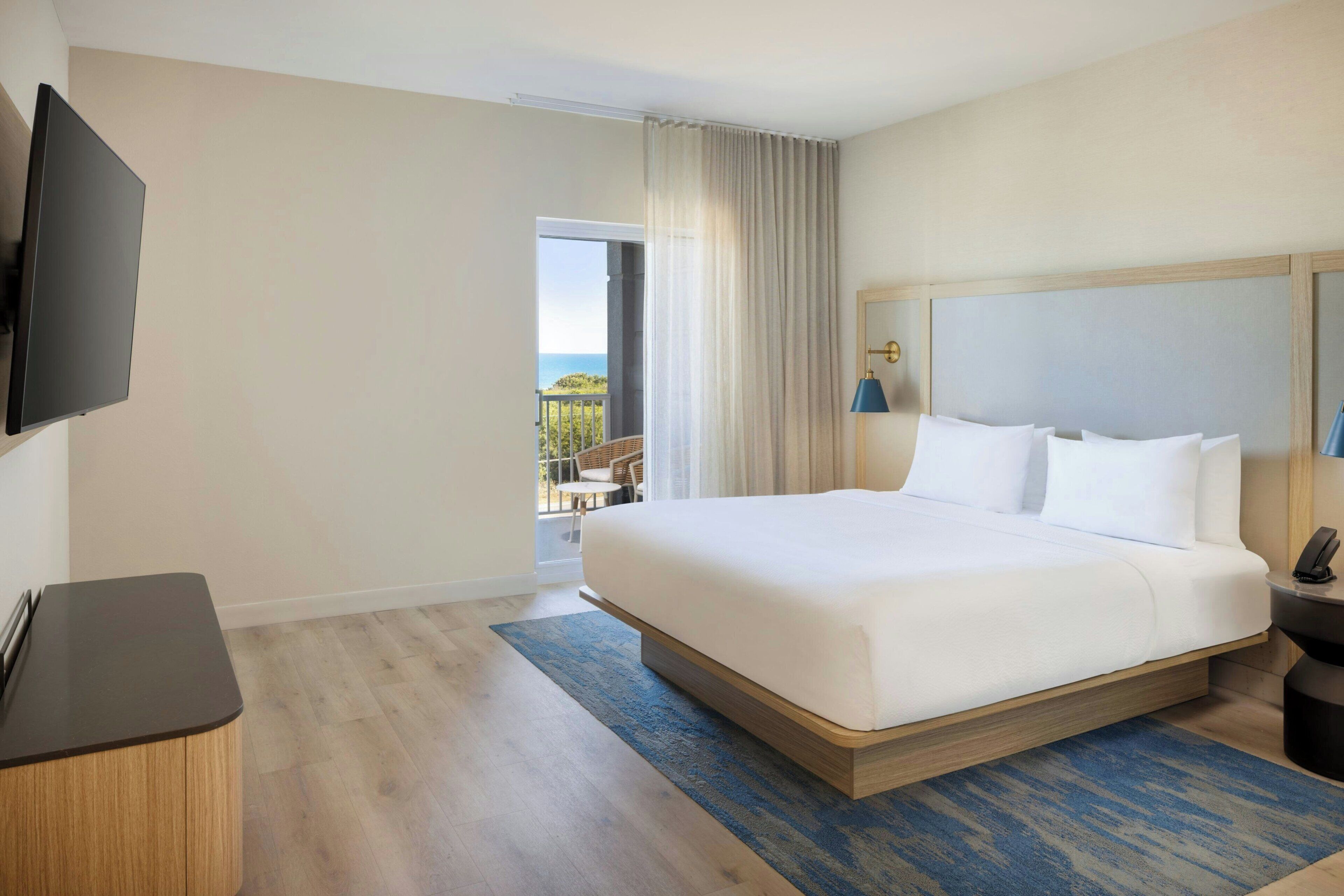 Quarto de hotel com cama grande, televisão, escrivaninha e vista para o exterior.