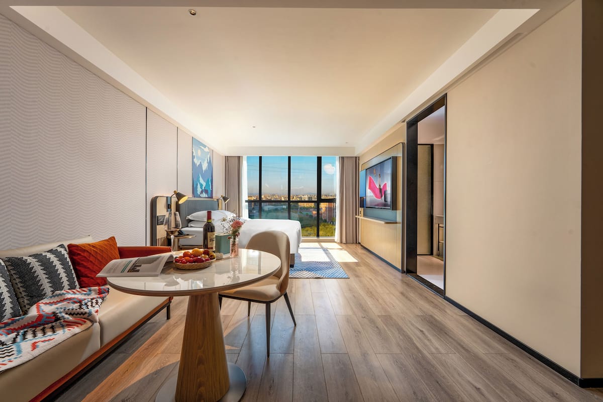 Quarto de hotel moderno com varanda, área de jantar e uma grande janela com vista para a cidade.