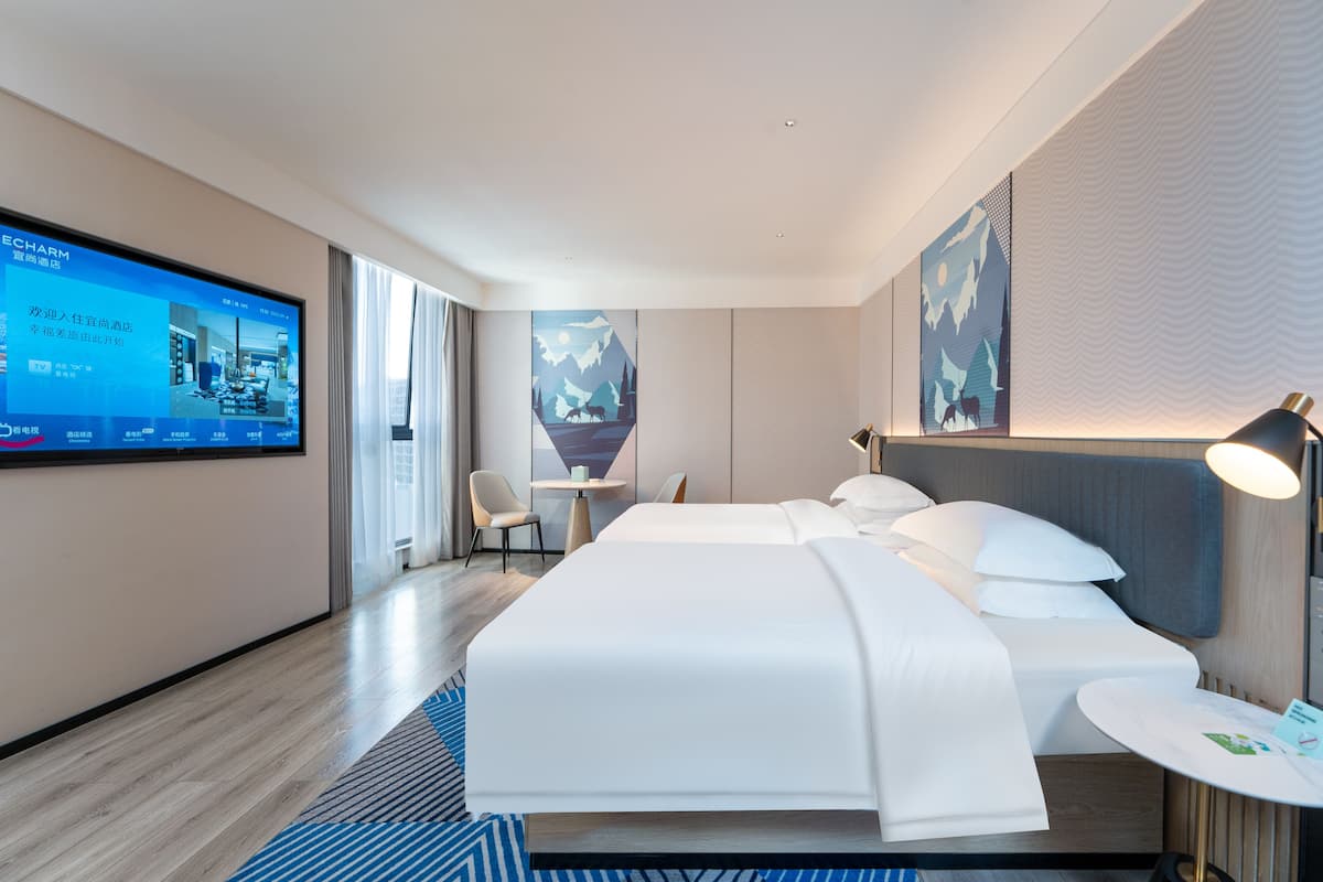 Quarto de hotel com uma cama grande, uma escrivaninha e uma televisão na parede.