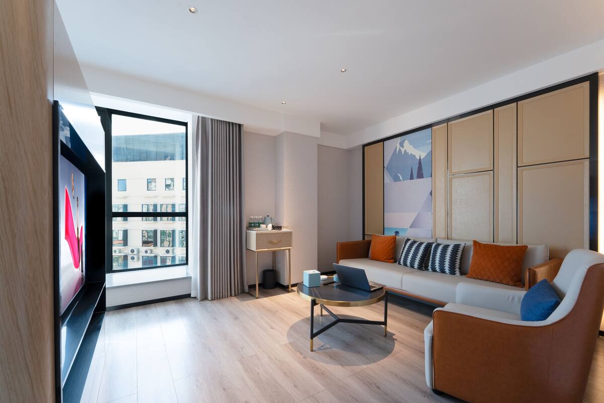 Quarto de hotel moderno com uma grande janela, um sofá, uma mesa de centro e uma televisão.
