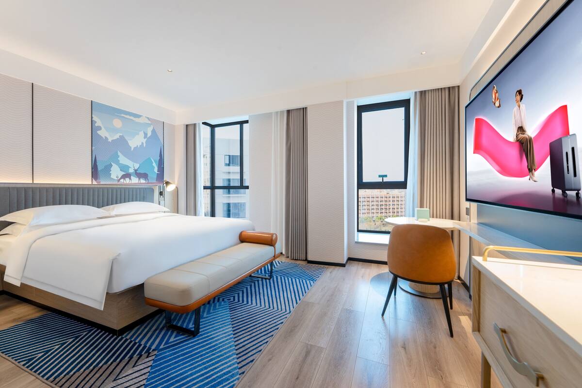 Quarto de hotel moderno com uma cama grande, uma escrivaninha, uma TV e vista para a cidade.