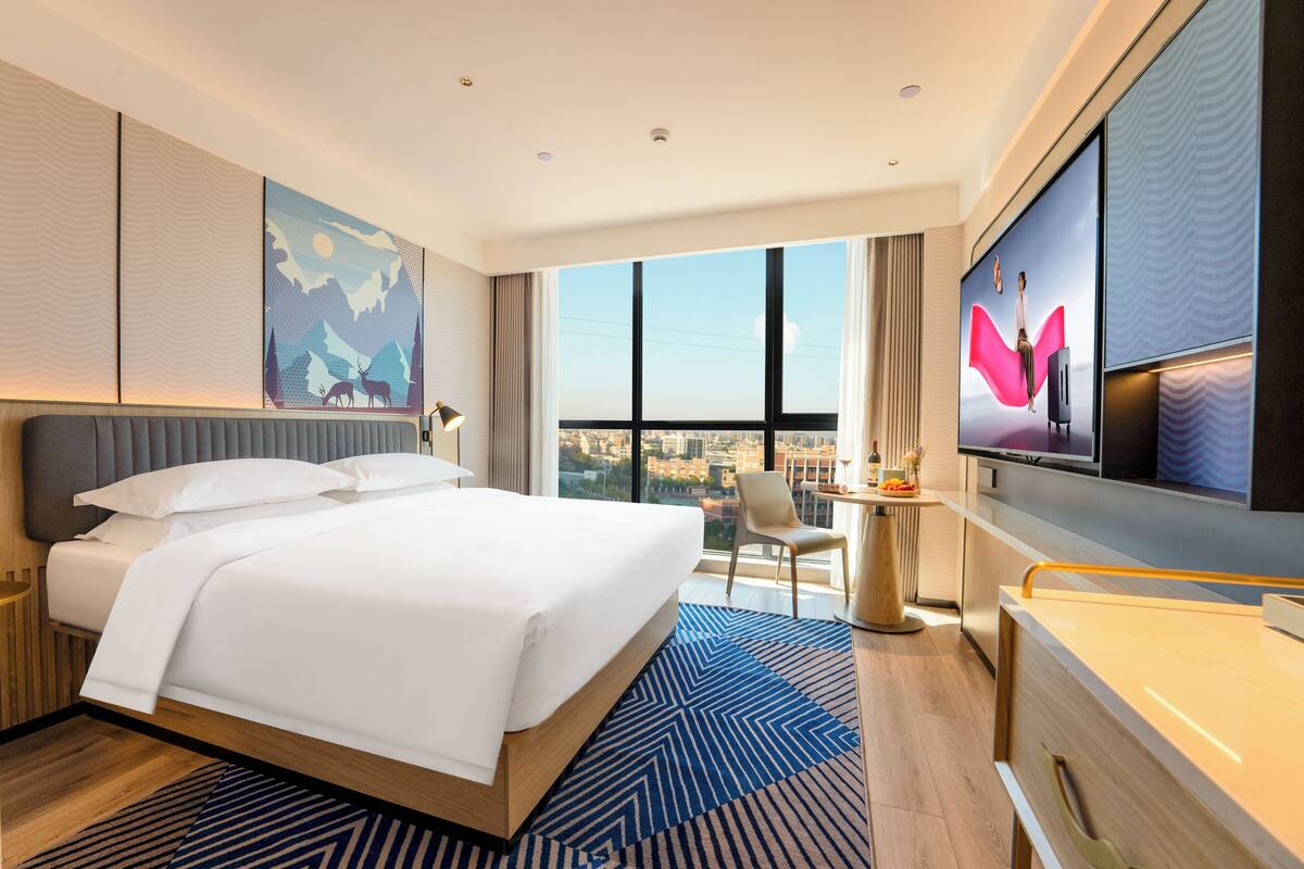 Quarto de hotel com uma cama grande, uma escrivaninha, uma televisão e vista para a cidade.