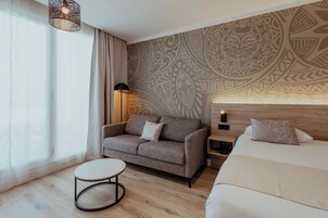 Quarto de hotel moderno com sofá, mesa de centro redonda, cama e parede com padrão.