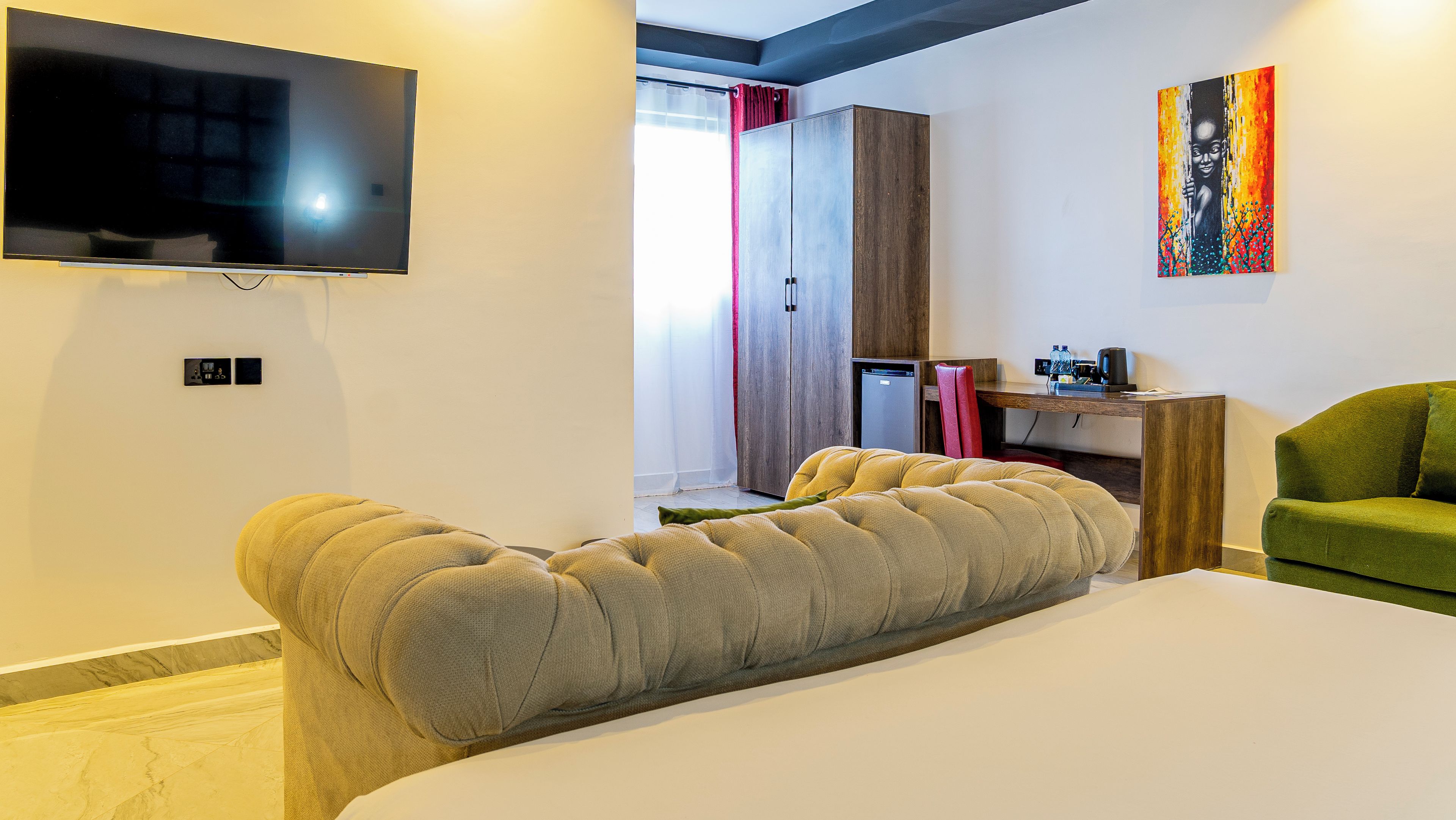 Quarto de hotel moderno com uma cama grande, televisão de tela plana, escrivaninha com cadeira e uma obra de arte colorida na parede.