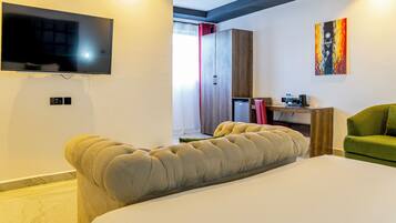 Quarto de hotel moderno com uma cama grande, televisão de tela plana, escrivaninha com cadeira e uma obra de arte colorida na parede.