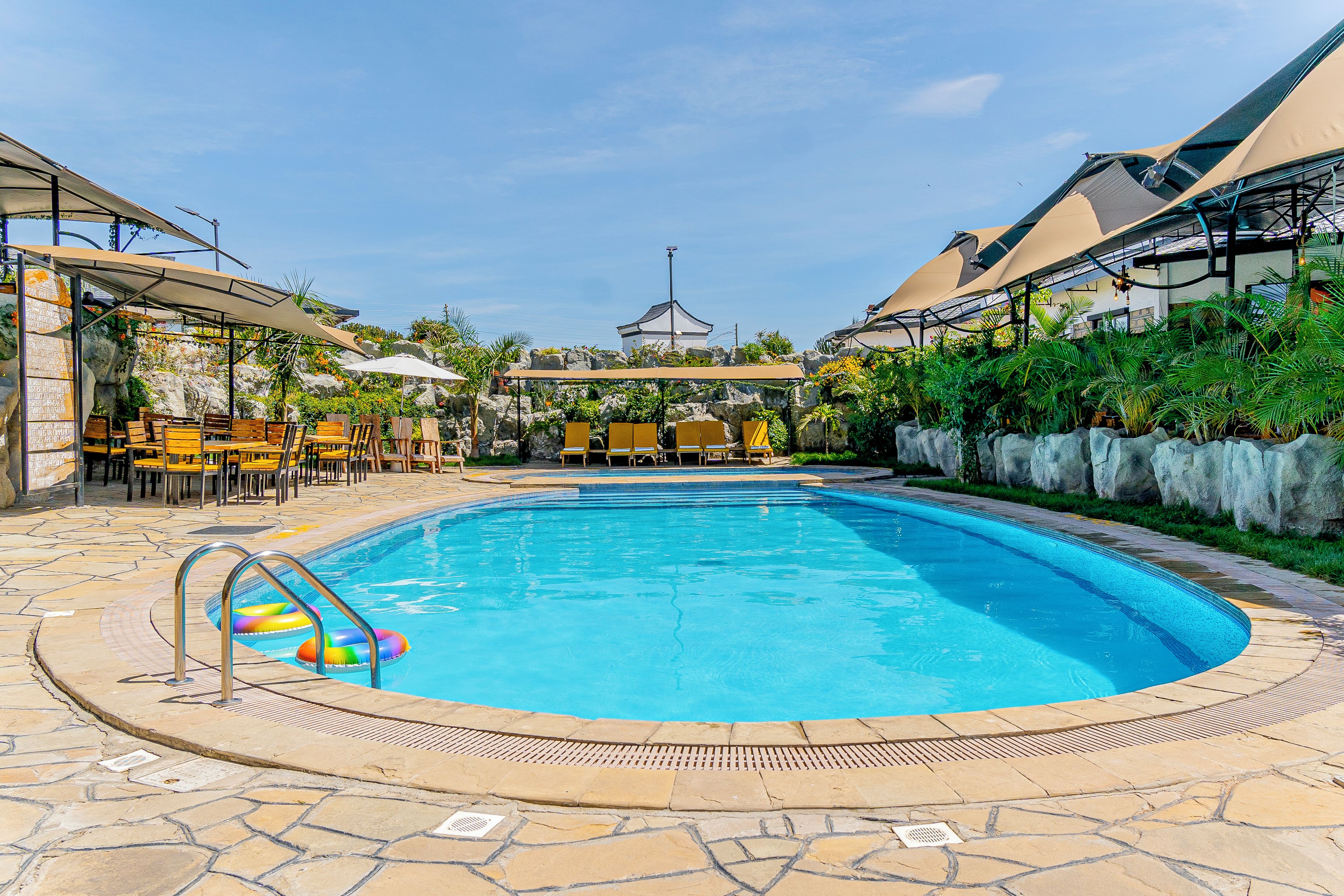 Piscina com deck de pedra, espreguiçadeiras e guarda-sóis.