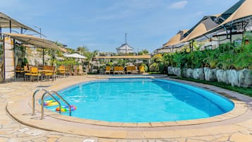 Piscina com deck de pedra, espreguiçadeiras e guarda-sóis.