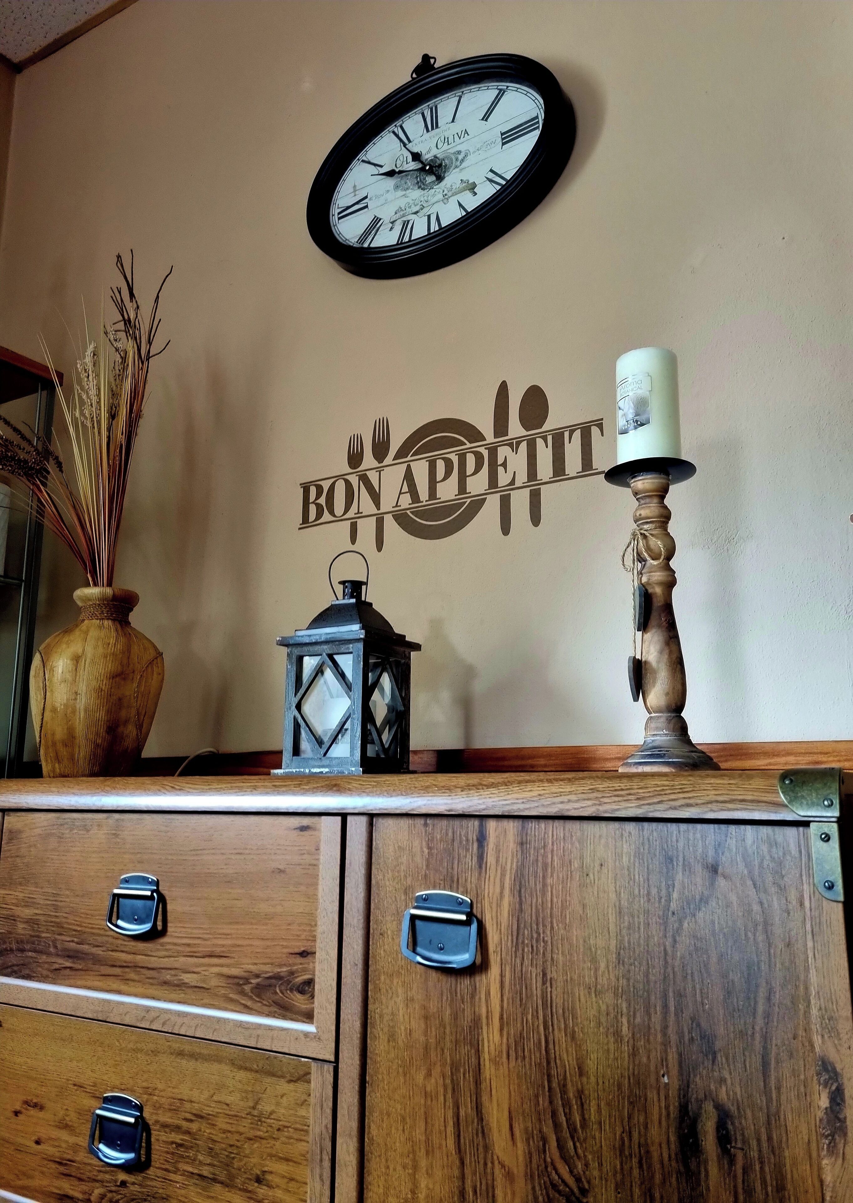 Um relógio de parede, um castiçal e uma placa decorativa com a inscrição 'BON APPETIT'.