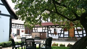 Um edifício tradicional de enxaimel com área de estar no jardim, com cadeiras pretas e uma mesa.