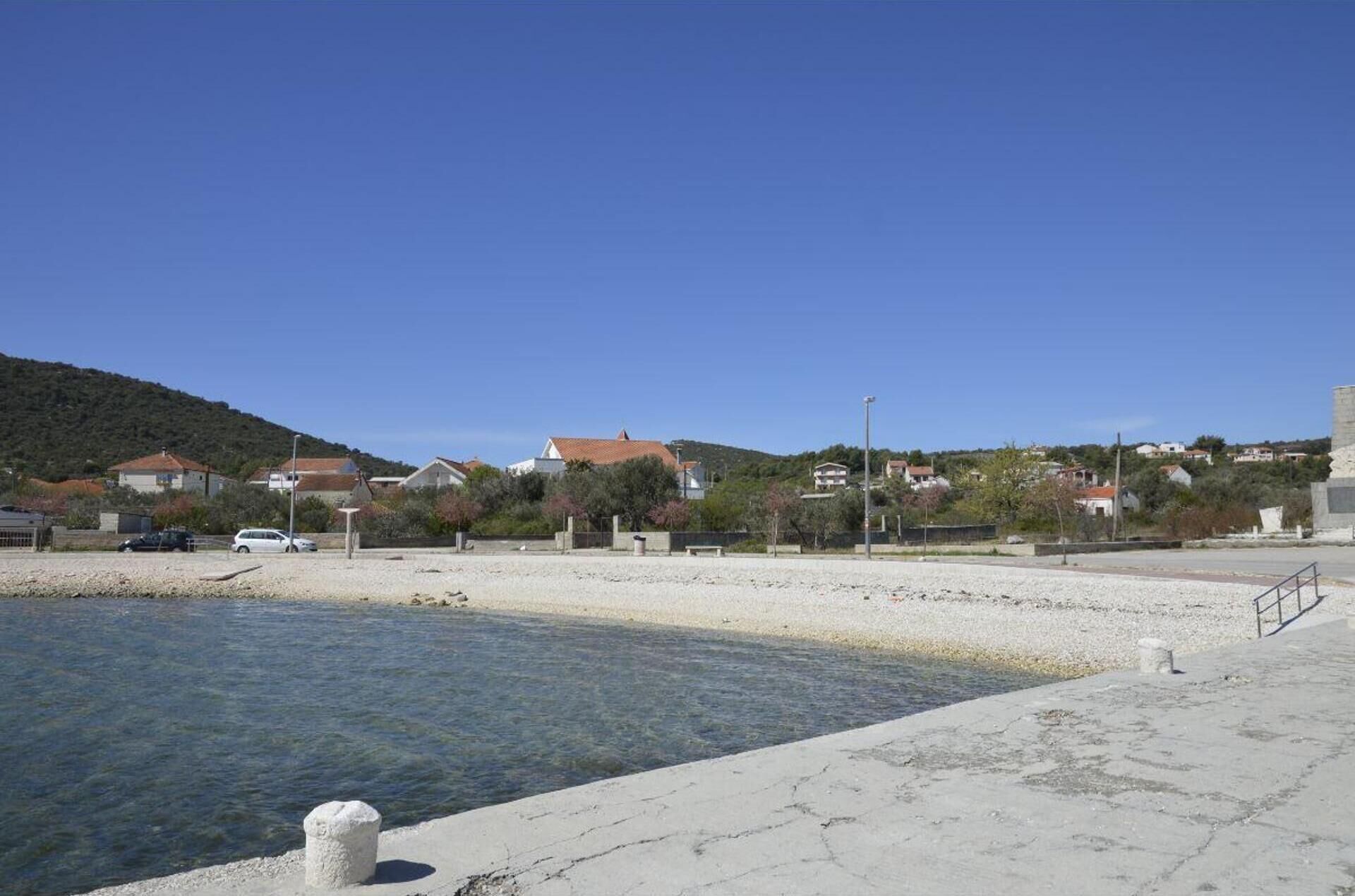 Uma área costeira com céu claro, uma praia de areia e edifícios residenciais ao fundo.