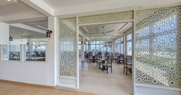 Uma sala de jantar ampla, com pé direito alto, janelas grandes e painéis decorativos.