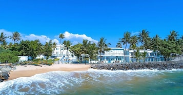 Uma propriedade à beira-mar com praia de areia, palmeiras e ondas do oceano.