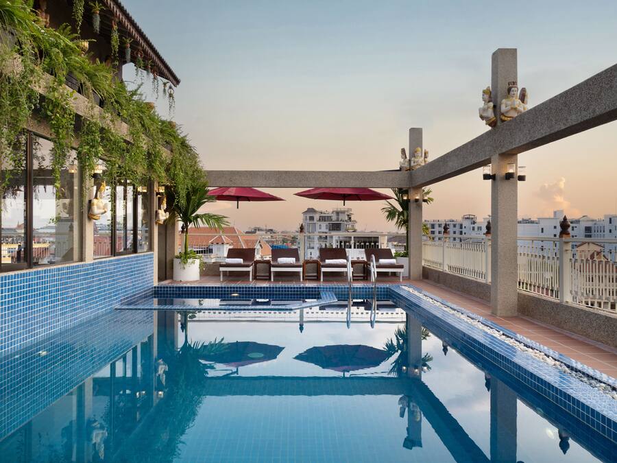 Uma piscina no terraço com água azul cristalina, rodeada por espreguiçadeiras e guarda-sóis, com vista para a cidade ao fundo.