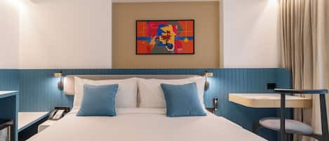 Quarto de hotel com cama, escrivaninha, cadeira, telefone e um quadro na parede.