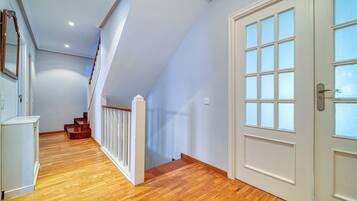 Um corredor com piso de madeira, uma porta branca com painéis de vidro e uma escada com corrimãos de madeira.