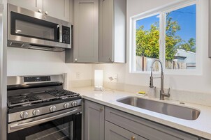 Cozinha com eletrodomésticos de aço inoxidável, pia dupla e janela com vista para árvores.