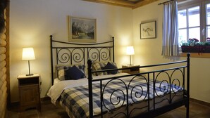 Quarto com estrutura de cama em metal, duas mesas de cabeceira com abajures, uma janela com cortinas e um quadro na parede.