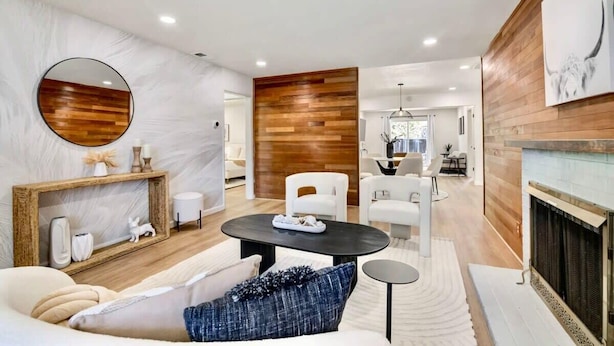 Uma sala de estar moderna com lareira, sofás brancos, uma mesa de centro e uma parede de destaque em madeira.