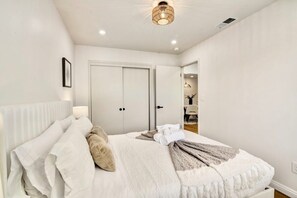 Quarto moderno com uma cama grande, um guarda-roupa e um banheiro visível por uma porta aberta.
