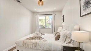 Quarto com cama, luminária de cabeceira, janela com cortinas e luminária no teto.