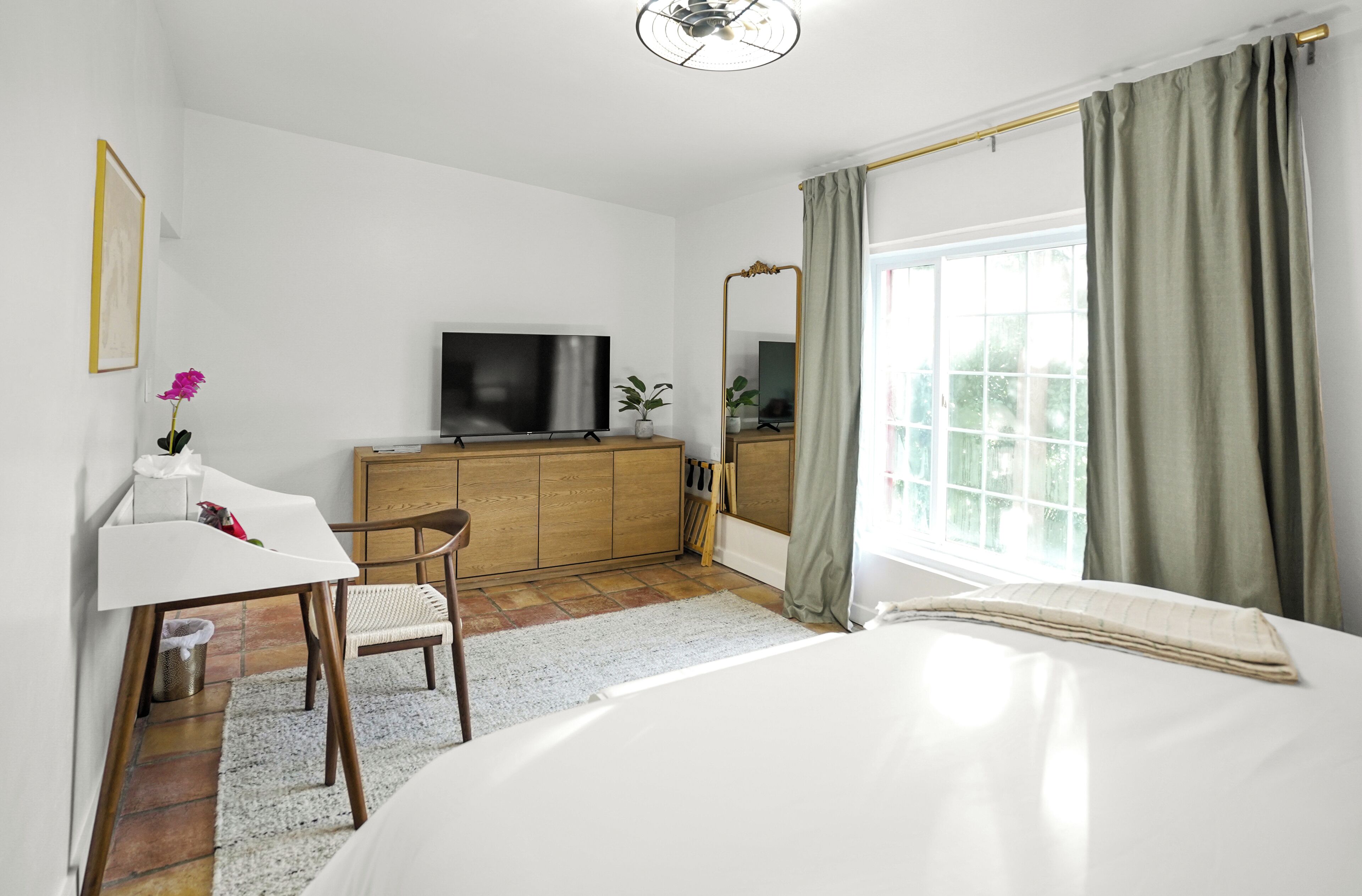 Quarto de hotel moderno com cama, escrivaninha, televisão e janela com cortinas.