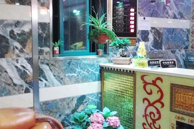 Uma área de recepção com paredes de mármore, uma planta em vaso, um painel decorativo e uma placa com caracteres chineses.
