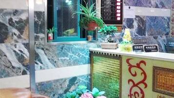 Uma área de recepção com paredes de mármore, uma planta em vaso, um painel decorativo e uma placa com caracteres chineses.