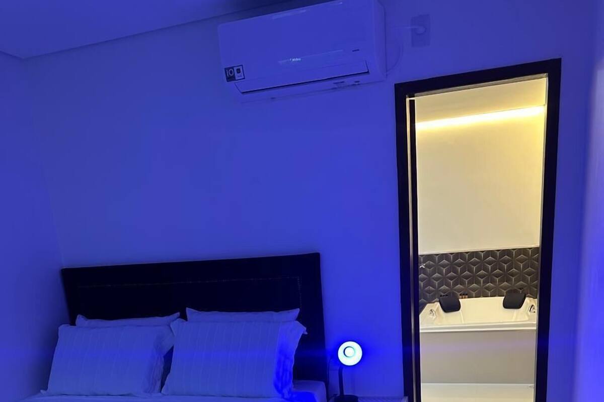 Quarto com cama, mesa de cabeceira e ar condicionado fixado na parede.