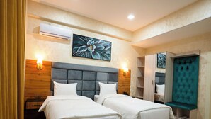 Quarto de hotel com duas camas, uma grande obra de arte na parede, ar condicionado e um guarda-roupa com espelho.