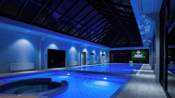 Piscina interior moderna com teto de vidro, hidromassagem e placa indicativa 'AVANT Swimming Pool'.