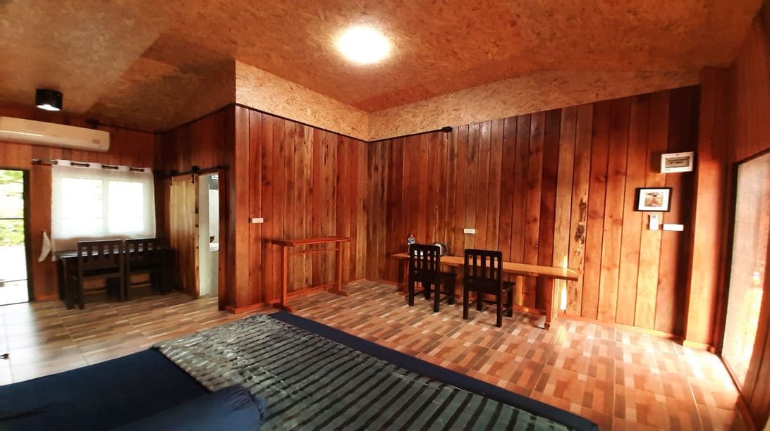 Quarto com paredes de madeira e chão de azulejos, com uma cama, escrivaninha e uma cadeira.