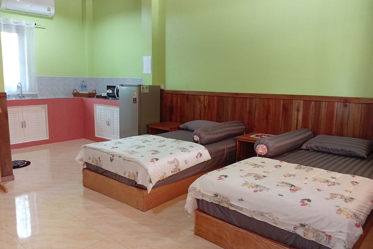 Quarto com duas camas, uma pequena cozinha e cabeceira de madeira.