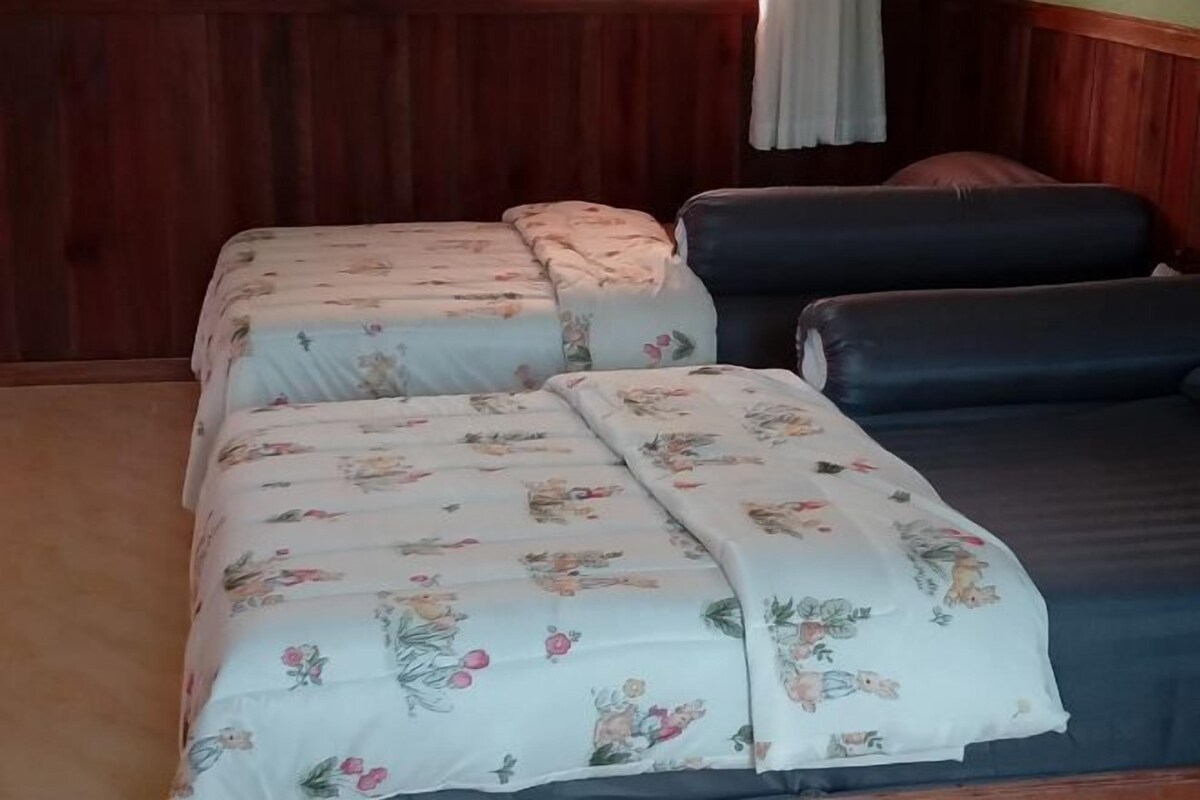 Um quarto com parede revestida de madeira, cama com roupa de cama floral e um sofá de cor escura.