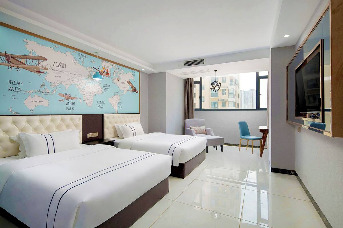 Quarto de hotel com duas camas, um mapa-múndi na parede, televisão e vista para a cidade.