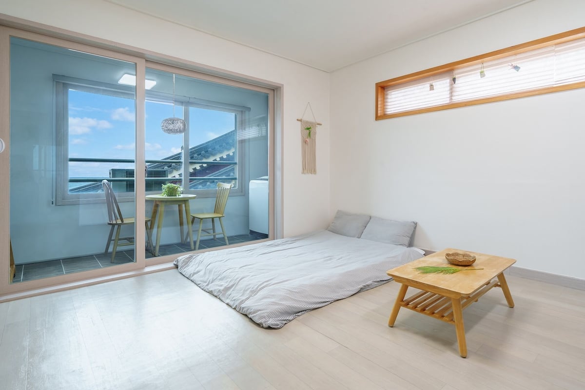 Quarto pequeno e luminoso com cama, mesa e varanda com vista.