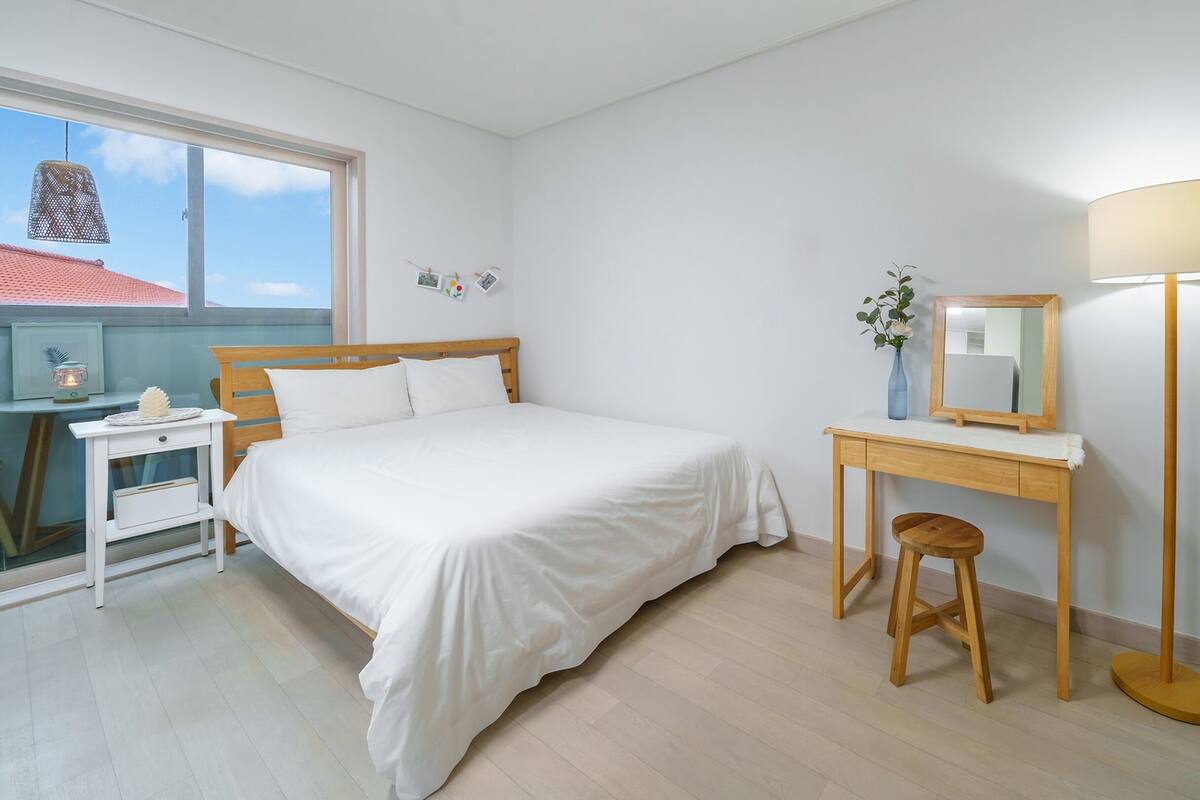 Quarto com cama, escrivaninha, cadeira, luminária e janela.