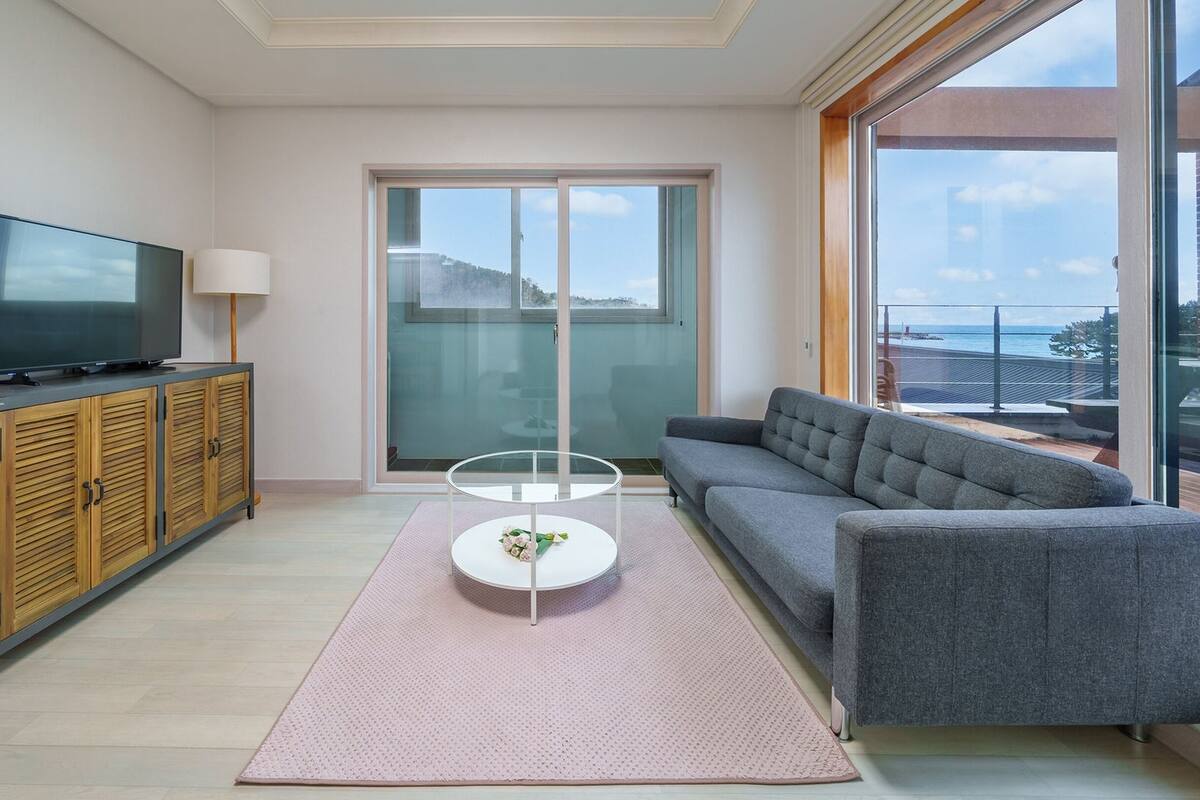 Uma sala de estar moderna com televisão de tela plana, armário de madeira, sofá cinza e mesa de vidro com um vaso.