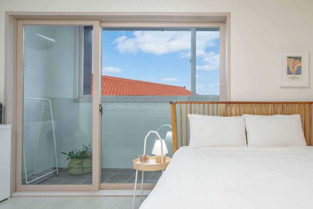 Quarto com cama, mesa de cabeceira, luminária, porta de vidro deslizante para uma varanda e um quadro na parede.
