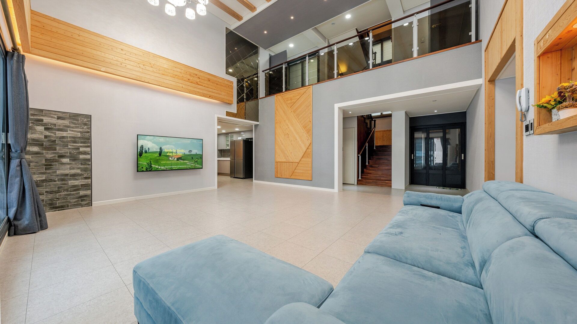 Uma sala de estar ampla com um sofá azul grande, uma TV de tela plana na parede e uma escada que leva a um andar superior.