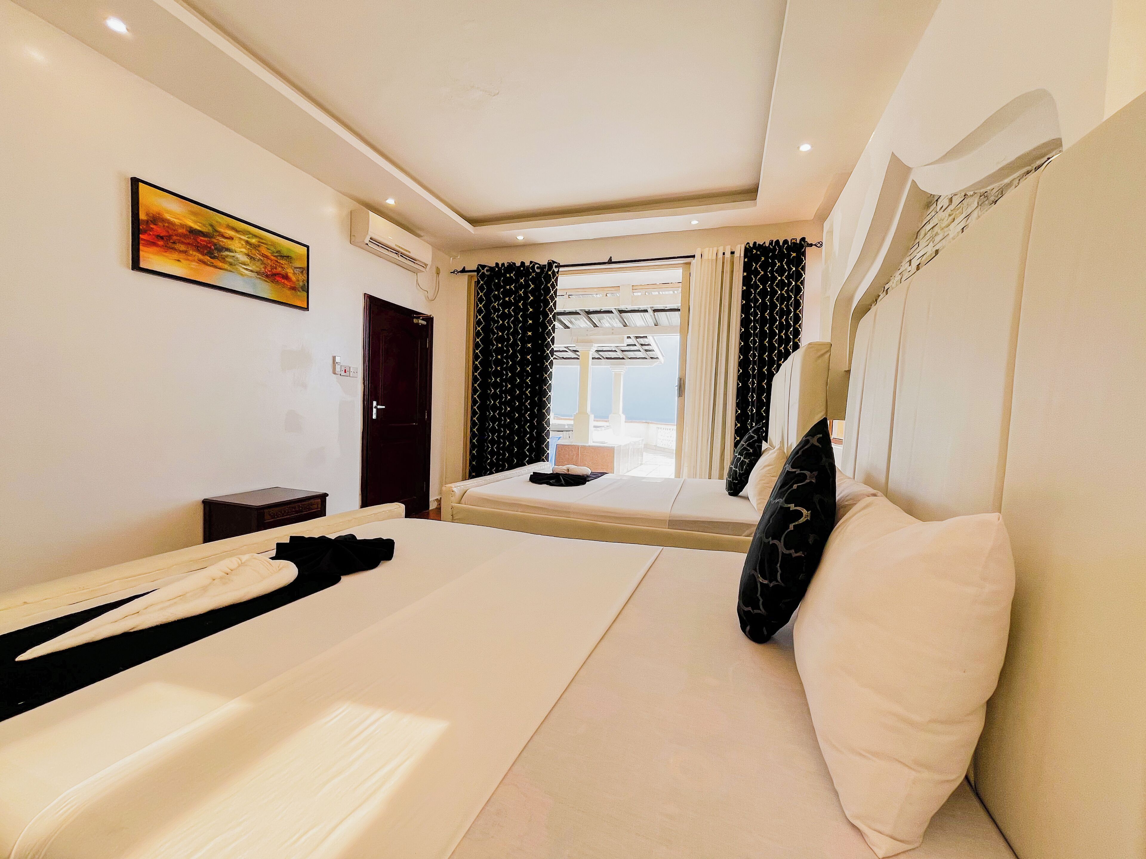 Quarto de hotel com duas camas, um quadro na parede, um aparelho de ar condicionado e vista para o exterior.