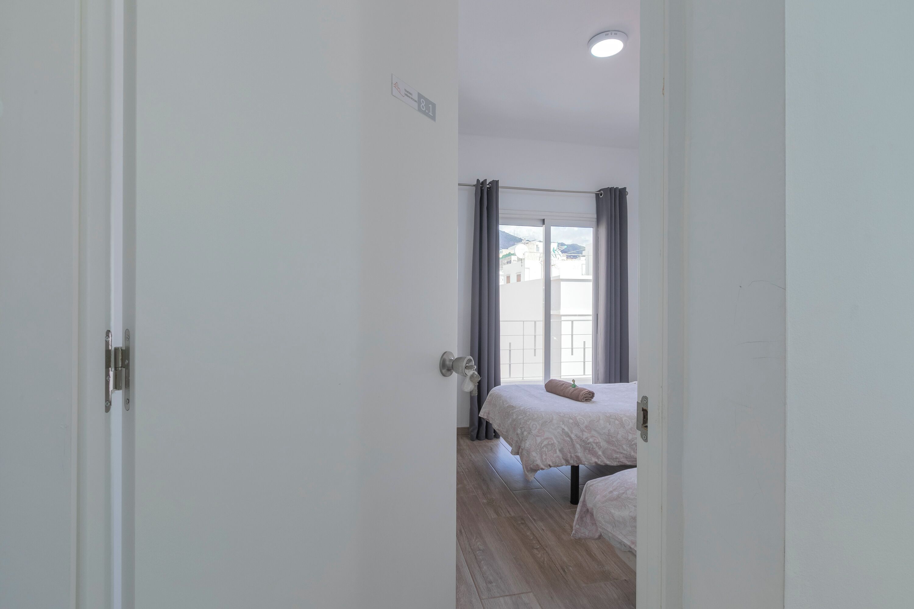 Quarto com cama, janela com cortinas e porta.
